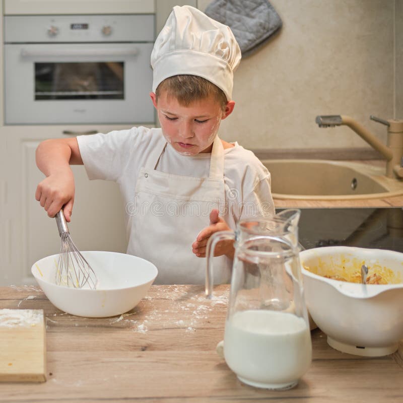 A Boy in Chef`s Clothes Whips Egg White with a Whisk for Cooking Apple ...