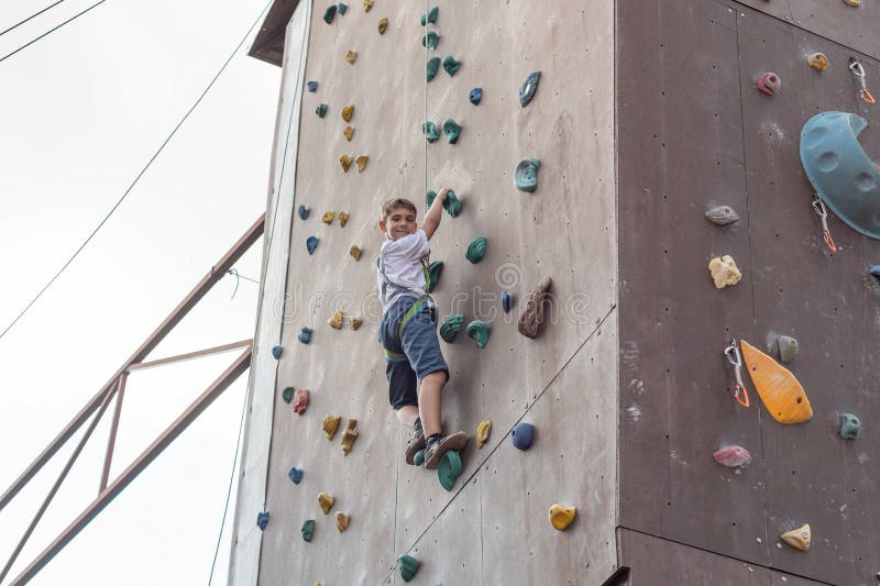 A Boy Climbs the Top of a Climbing Wall in a Sports Park Climbing Wall ...