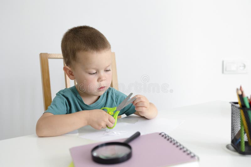 The Boy Cuts Out Shapes from White Paper with Scissors. Stock Photo ...