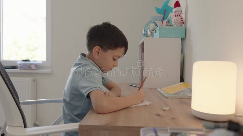 Young Boy Doing Homework at His Desk in His Room at Home, Pencil in Hand Writing in Notebook ...