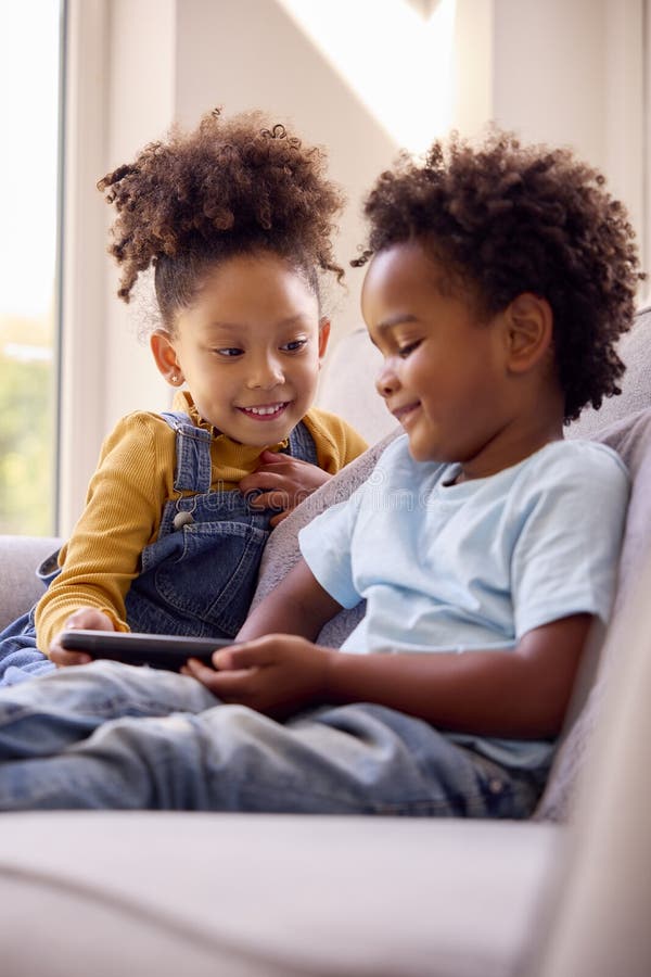 Boy and Girl Playing Handheld Computer Game Sitting on Sofa at Home ...