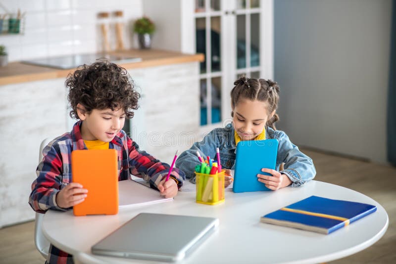 Boy and Girl Sitting at Round Table, Holding Tablets, Writing Stock ...