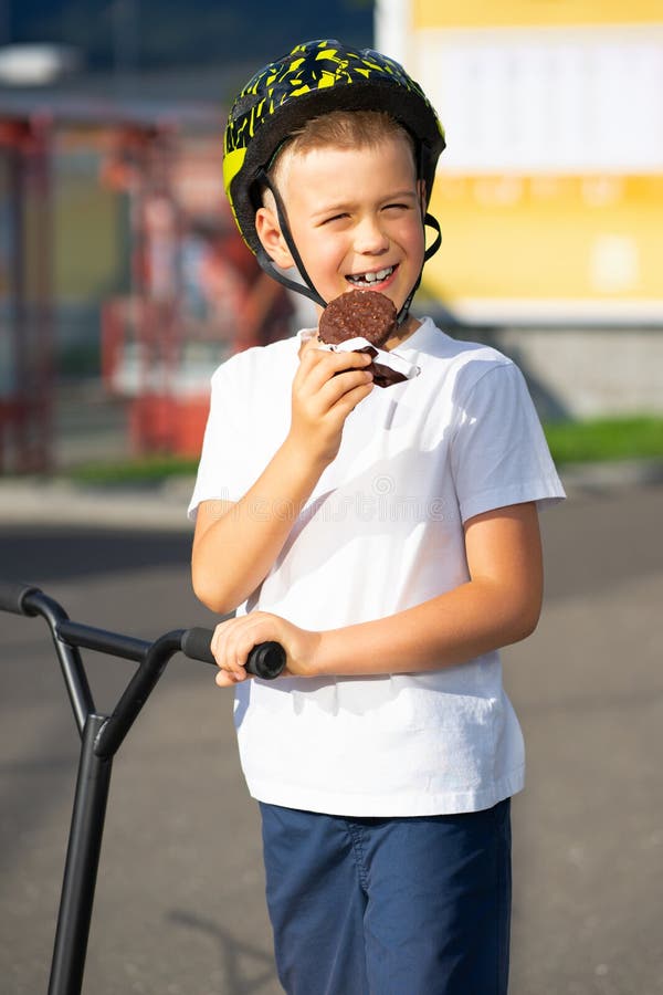 A Boy in a Helmet and on a Scooter Eats Ice Cream during a Break from ...