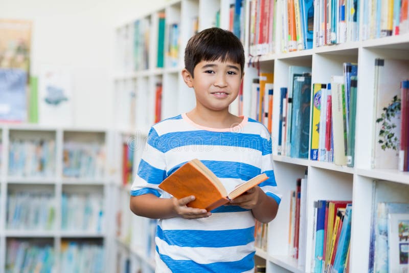 Asian Boy Reading Orange Book while Standing in Library Aisle between ...