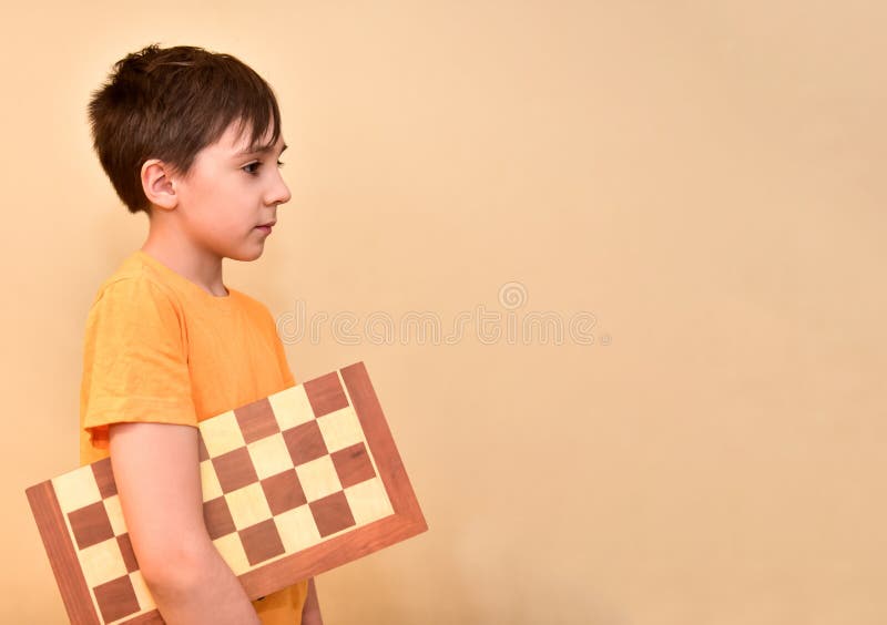 A Boy Holds a Chessboard in His Hands and Looks at it, Posing Emotional ...