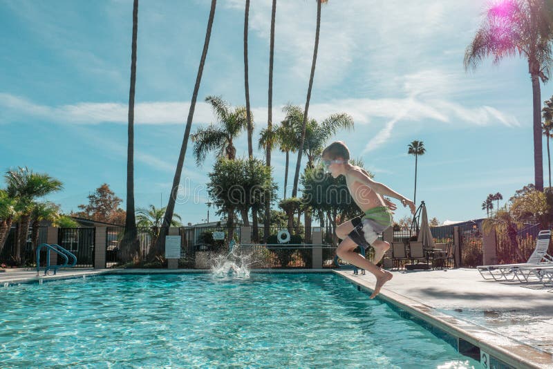 Boy Jumping into the Pool Surrounded by Palm Trees Under Sunlight and a ...