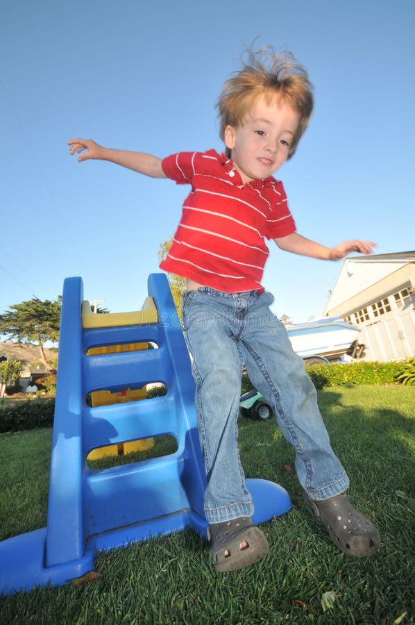 Boy Jumps Off a Slide Onto the Grass Stock Photo - Image of slide ...