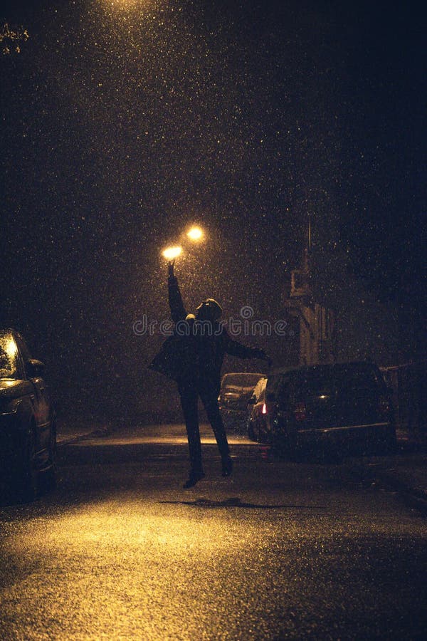 A Boy Jumps To Reach the Light at Night during a Heavy Snowfall Stock ...