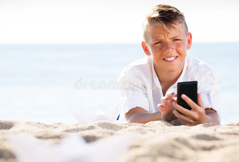 Boy Looking at Phone while Resting on Beach Stock Image - Image of ...
