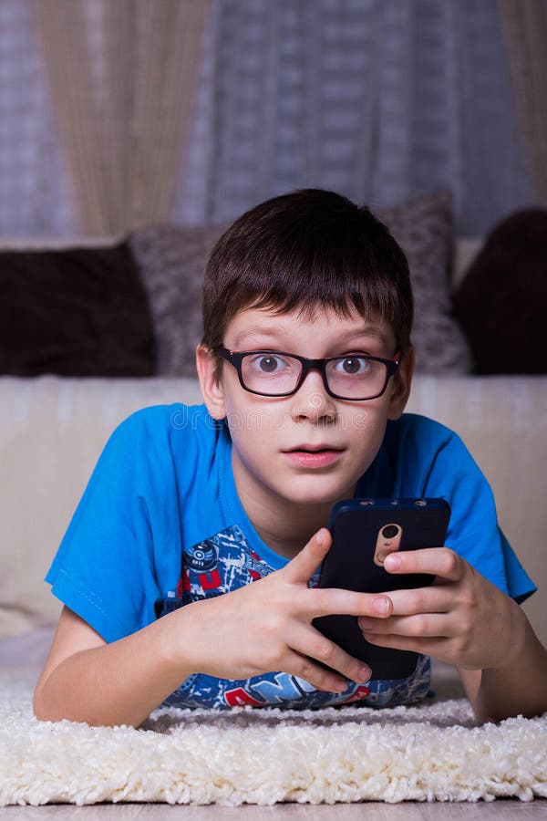 The Boy is Lying on the Floor, Holding a Smartphone and Looking at the ...