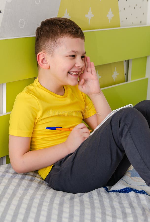 The Boy Makes Notes on a Paper Tablet, Sitting in His Room on the Bed ...