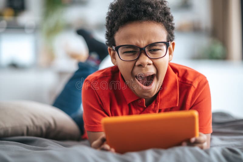 A Boy in Orange Tshirt Watching Something Online and Yawning Stock ...