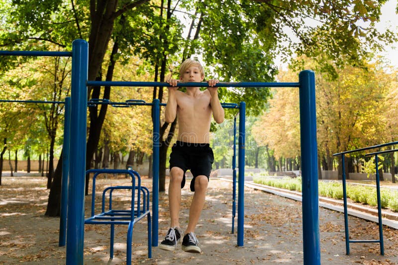 A Boy Performs Pull-ups in the Park. Athletic Teenage Boy in the Park ...