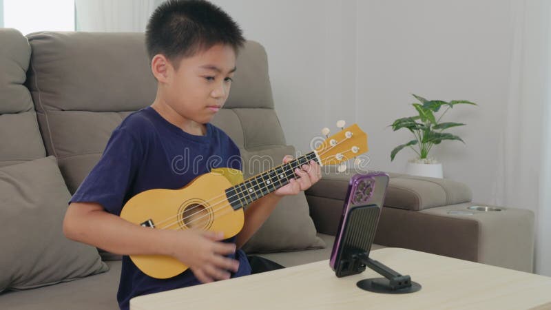 A Young Boy Sits on a Couch Playing a Ukulele, Streaming an Online ...