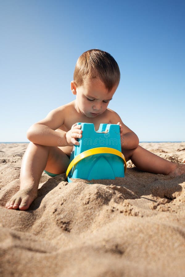 A Boy Plays in the Sand with a Blue Bucket To Build a Sand Castle Stock ...