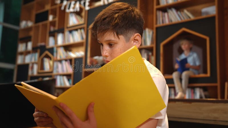 Boy Reading a Book while Group of Smart Students Sitting at Library ...