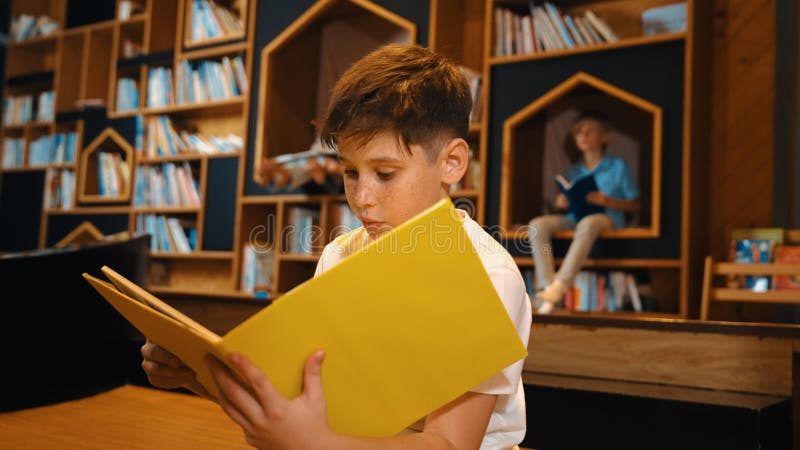 Boy Reading a Book while Group of Smart Students Sitting at Library ...