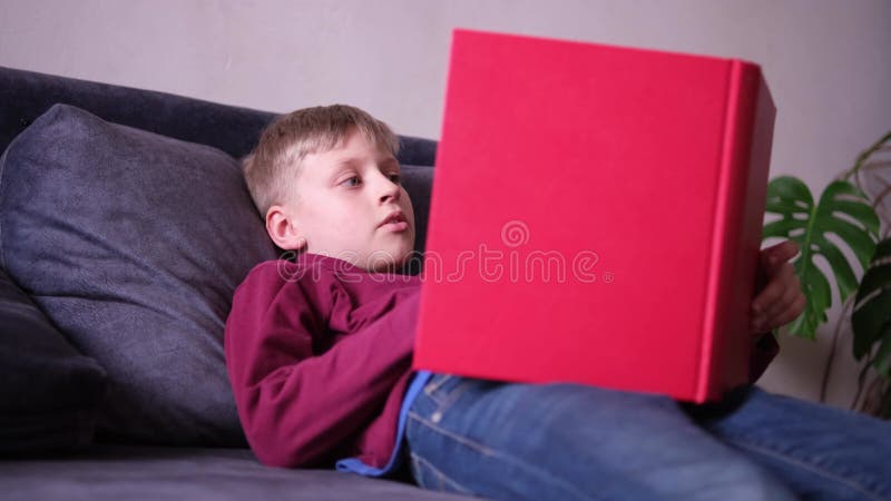 Boy Reading a Book. a Young Boy Lying on a Couch and Reading a Large ...