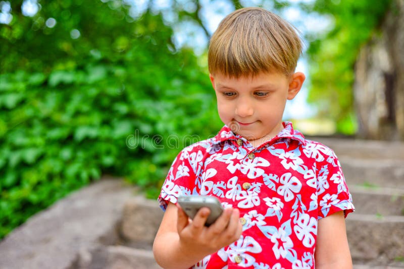 A Boy in Red Clothes is Looking at the Phone while Standing in the Park ...