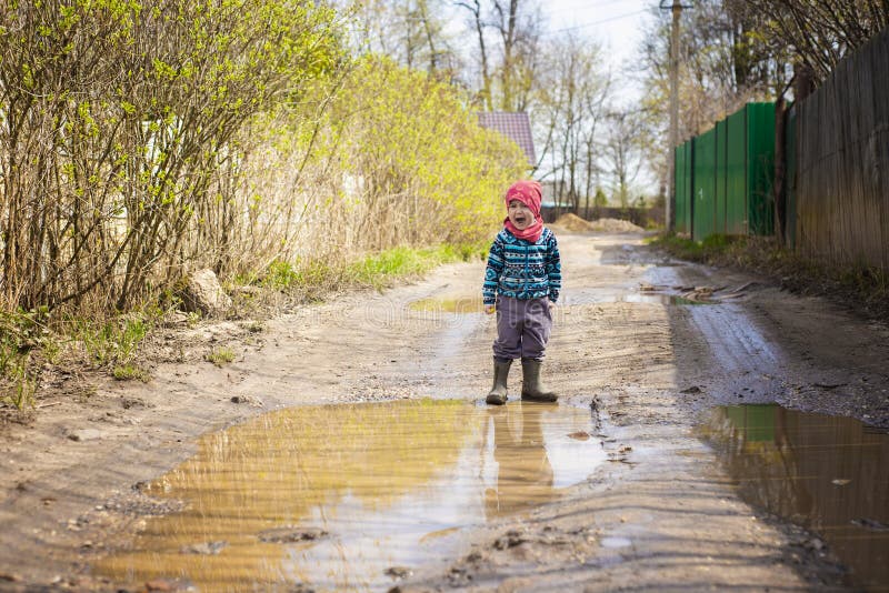 A Boy in a Red Hat and Rubber Boots Crying, Afraid of Puddles, Jumps ...