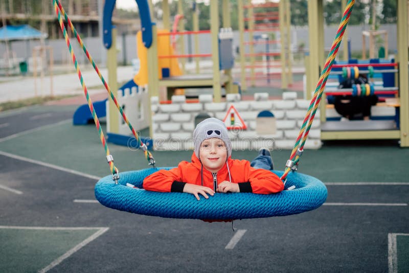 A Boy in a Red Jacket is Swinging on a Swing in the Playground. Stock ...