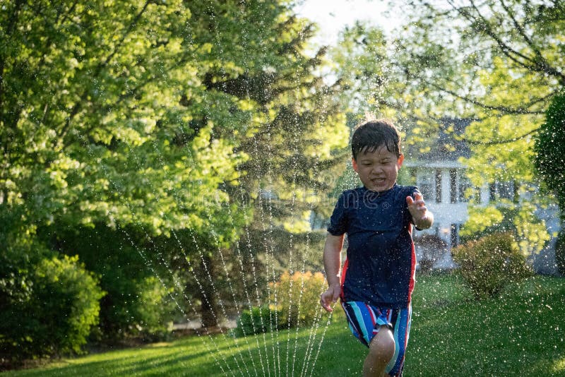 Boy Running through Sprinklers in Backyard Stock Photo - Image of ...