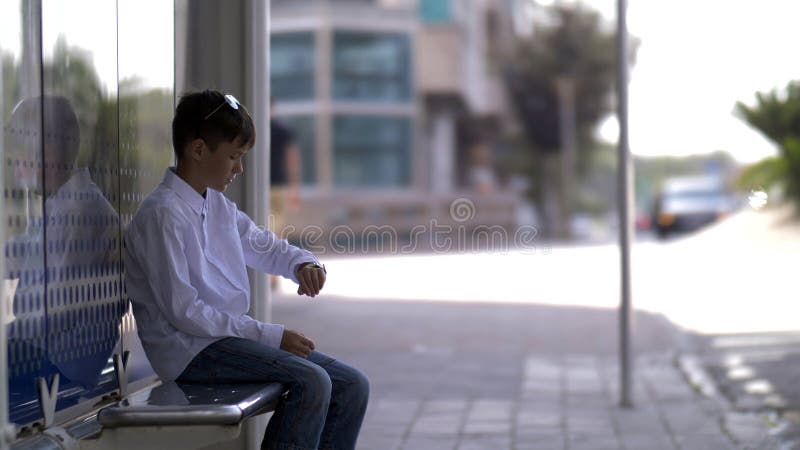 Boy Sits at the Bus Stop and Looks at Watch Stock Image - Image of ...