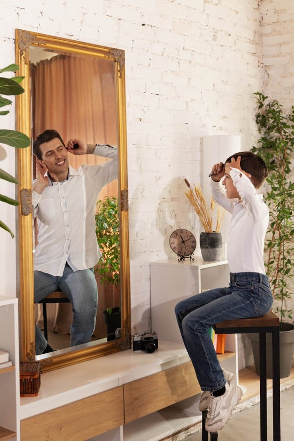 Boy Sits on Stool, Combing His Hair in Front of Large Mirror, while His ...