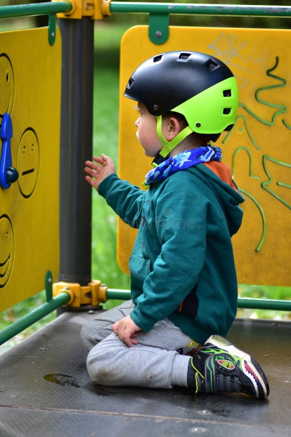 Boy Sitting Cross-legged on Playground Platform, Helmet on, Exploring Yellow Activity Panels ...