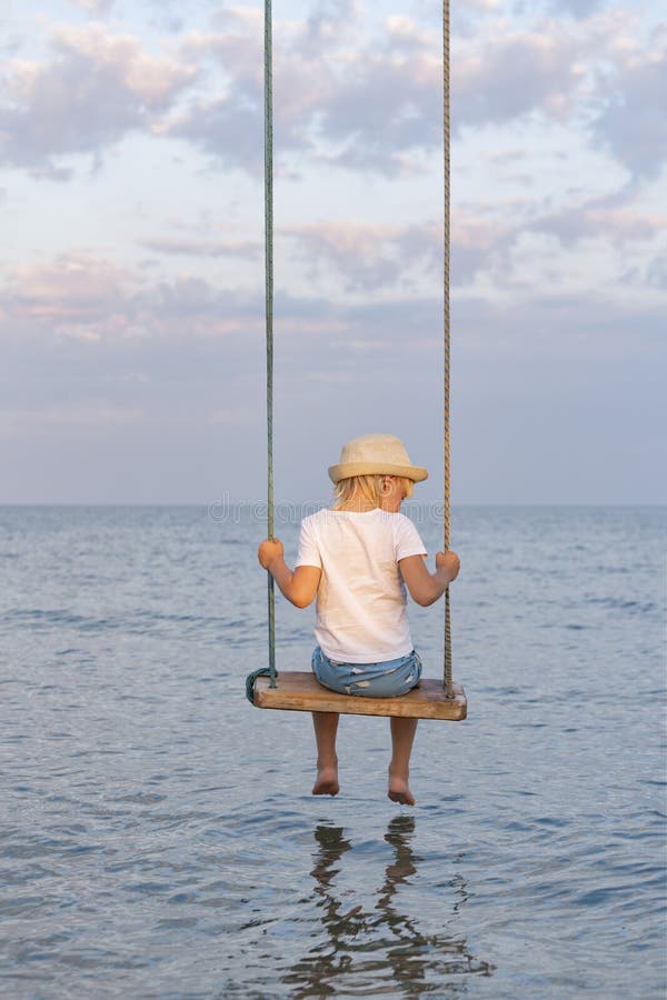Boy Sitting on Rope Swing Over the Water. Swing on Beach Stock Photo ...