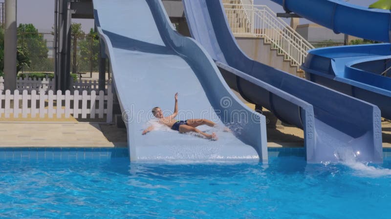 Boy Slides Down a Water Slide into a Sparkling Pool with Joy Stock ...