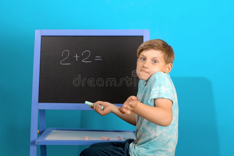 The Boy Solves the Math Equation 2 + 2 Written on the Blackboard. the ...