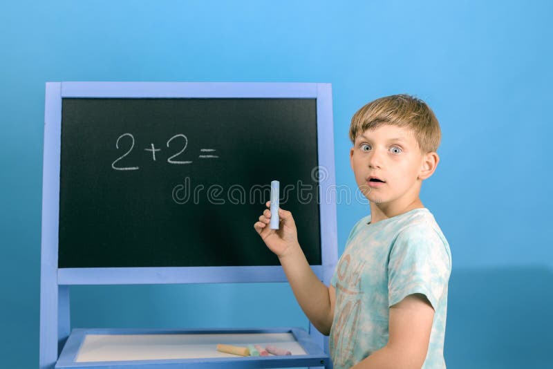 The Boy Solves the Math Equation 2 + 2 Written on the Blackboard. the ...