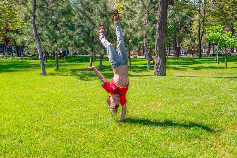 A Boy Stands on One Arm Upside Down in a Park on Green Grass Stock ...