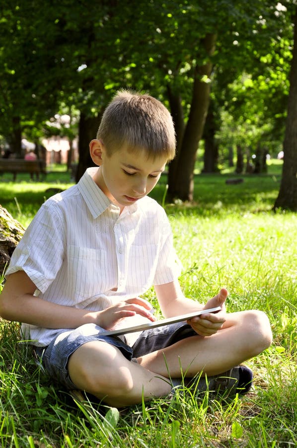 Little Boys Sitting on the Grass in a Park and Using Tablet PC ...