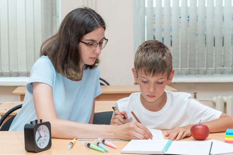 A Boy and a Teacher Doing Homework, Writing Text in a Notebook at the ...