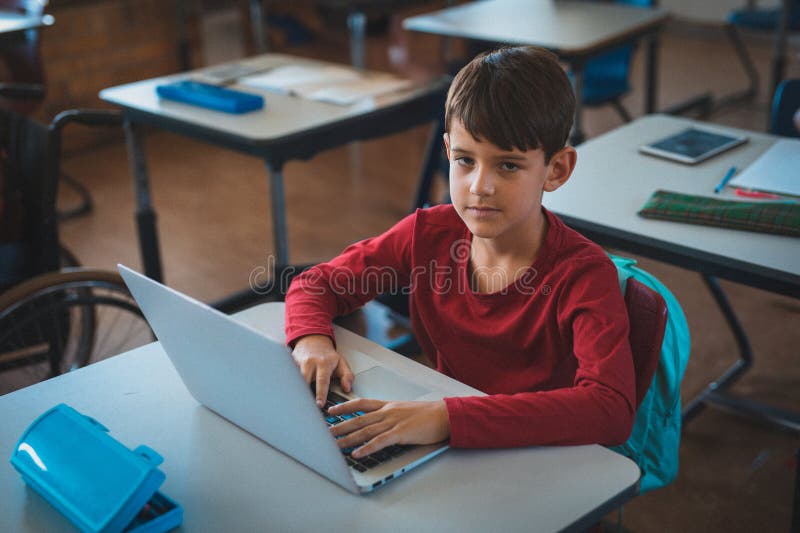 Boy Typing on Silver Laptop at School Desk in Classroom, with Blue ...