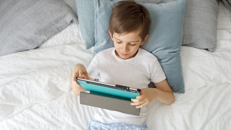 A Boy Using a Tablet Computer while Lying in Bed during the Day. His ...