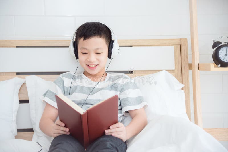 Boy Wearing Headset and Reading Book on Bed Stock Photo - Image of ...