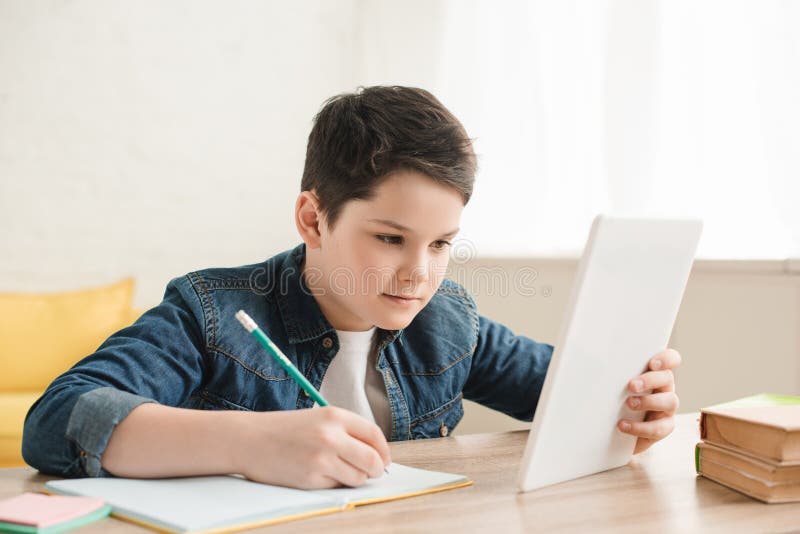 Boy Writing in Notebook and Using Digital Table while Doing Schoolwork ...