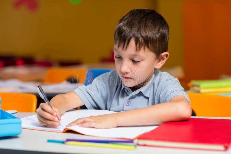 Boy Writing at School Desk in Elementary Classroom, with Pen Open ...