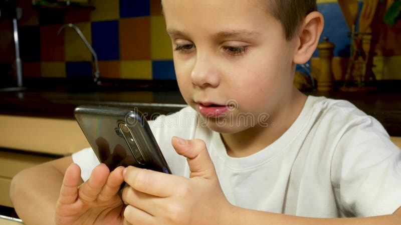 A Boy in the Kitchen with a Phone in His Hands Taps the Screen and ...