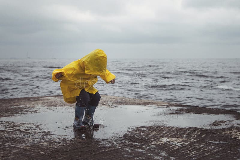 A Boy in a Yellow Raincoat Jumps on Puddles. Stock Photo - Image of ...