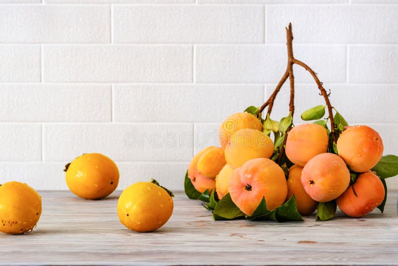 A Branch of Ripe Persimmons on a Wooden Table Against a Background of a ...