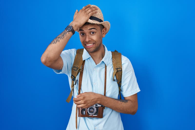 Brazilian Young Man Holding Vintage Camera Surprised With Hand On Head For Mistake Remember