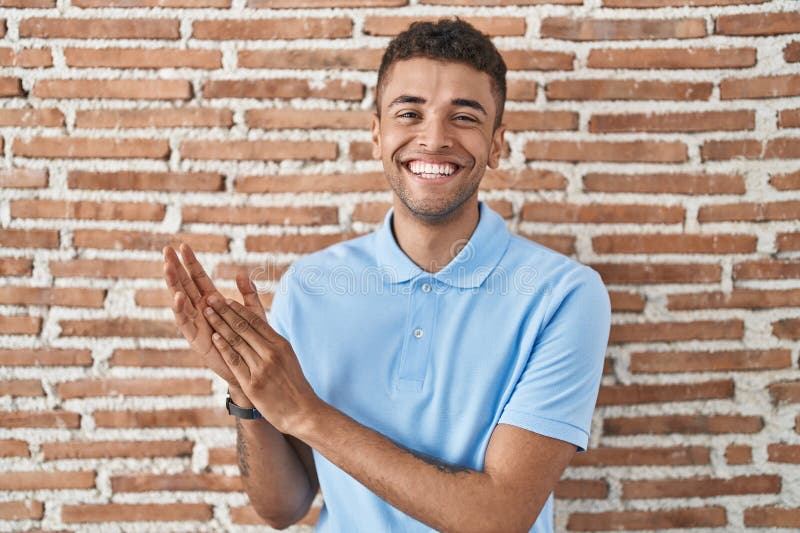 Brazilian Young Man Standing Over Brick Wall Clapping And Applauding