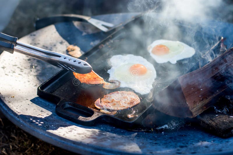 Camp Cooking. Grilling Crispy Bacon and Eggs on a Cast Iron Plate Over ...