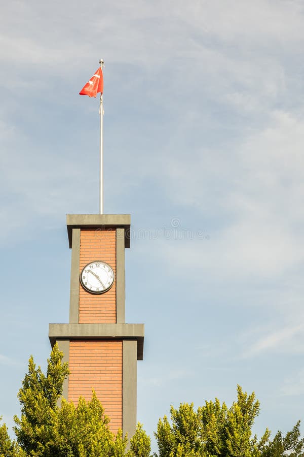 Brick Clock Tower with Flag Against Blue Sky Surrounded by Trees Stock ...