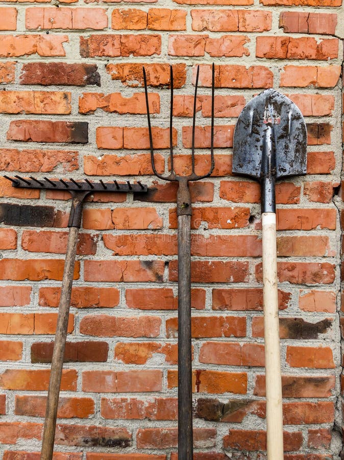 A Brick Wall with Three Garden Tools Leaning Against it Stock Photo ...