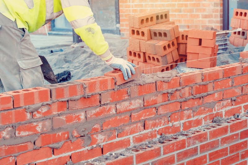 Bricklayer in Safety Vest and a Helmet Laying a Brick Wall Using a ...